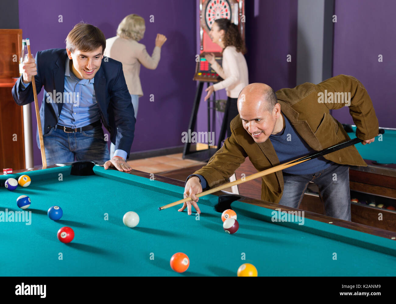 Group of charming positive friends playing billiards and smiling in ...