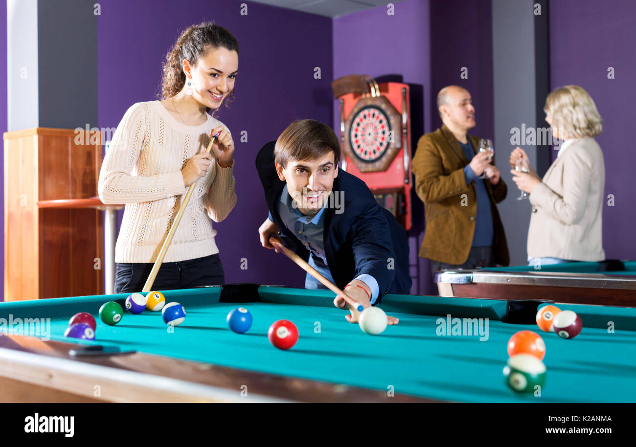 Happy group of friends playing billiards and smiling in billiard club ...