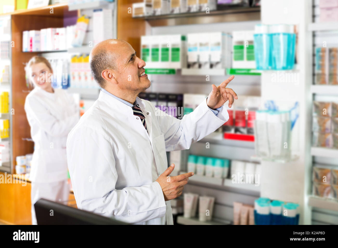 Positive mature pharmacist and female assistant working at farmacy ...