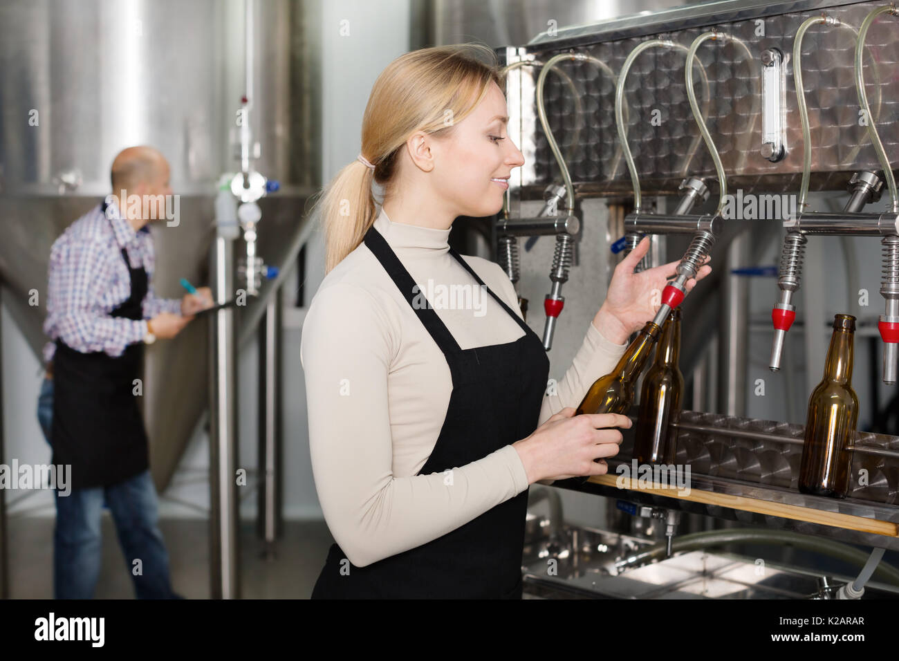 Young cheerful woman wearing uniform using a bottling equipment on a ...