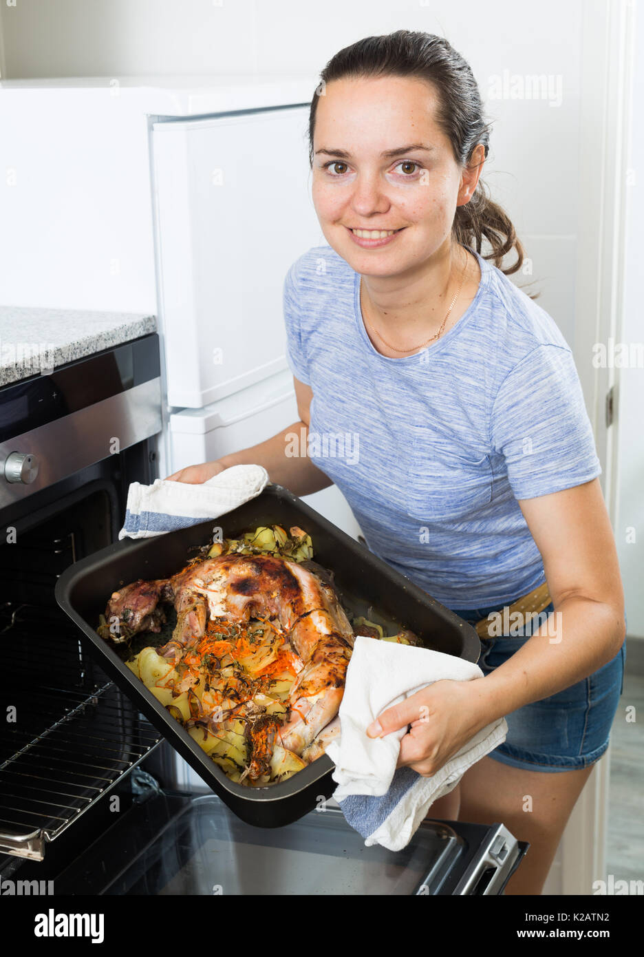 portrait of cheerful young woman cooking roasted meat in oven on ...