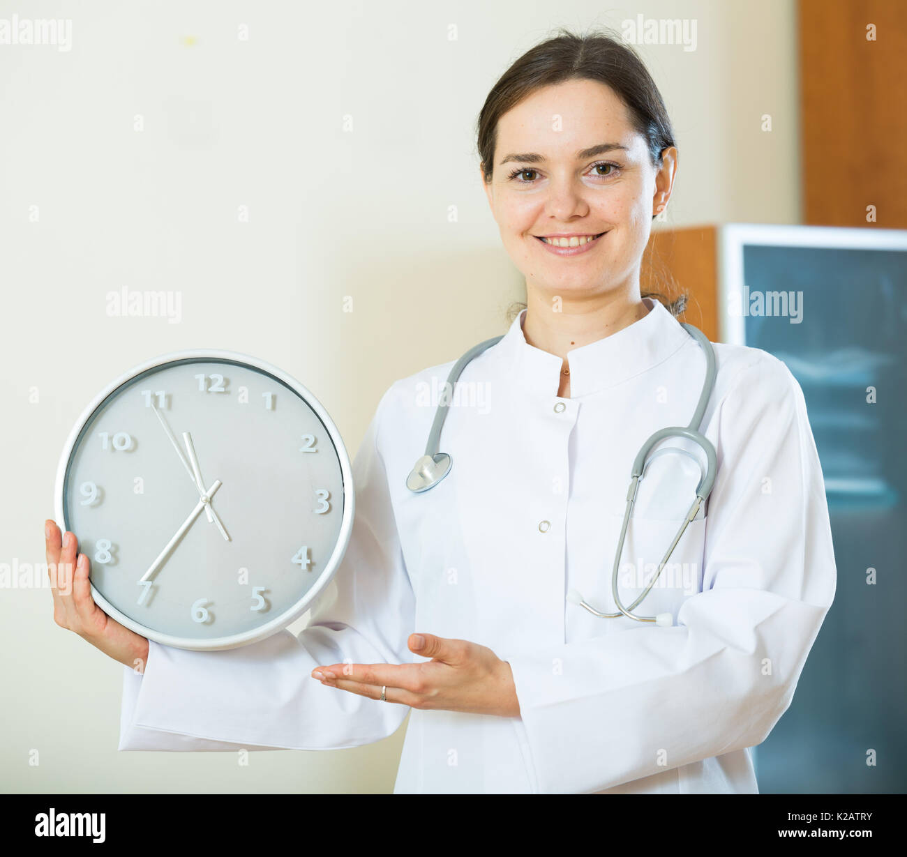 Female physician with stethoscope showing clock with schedule of work ...