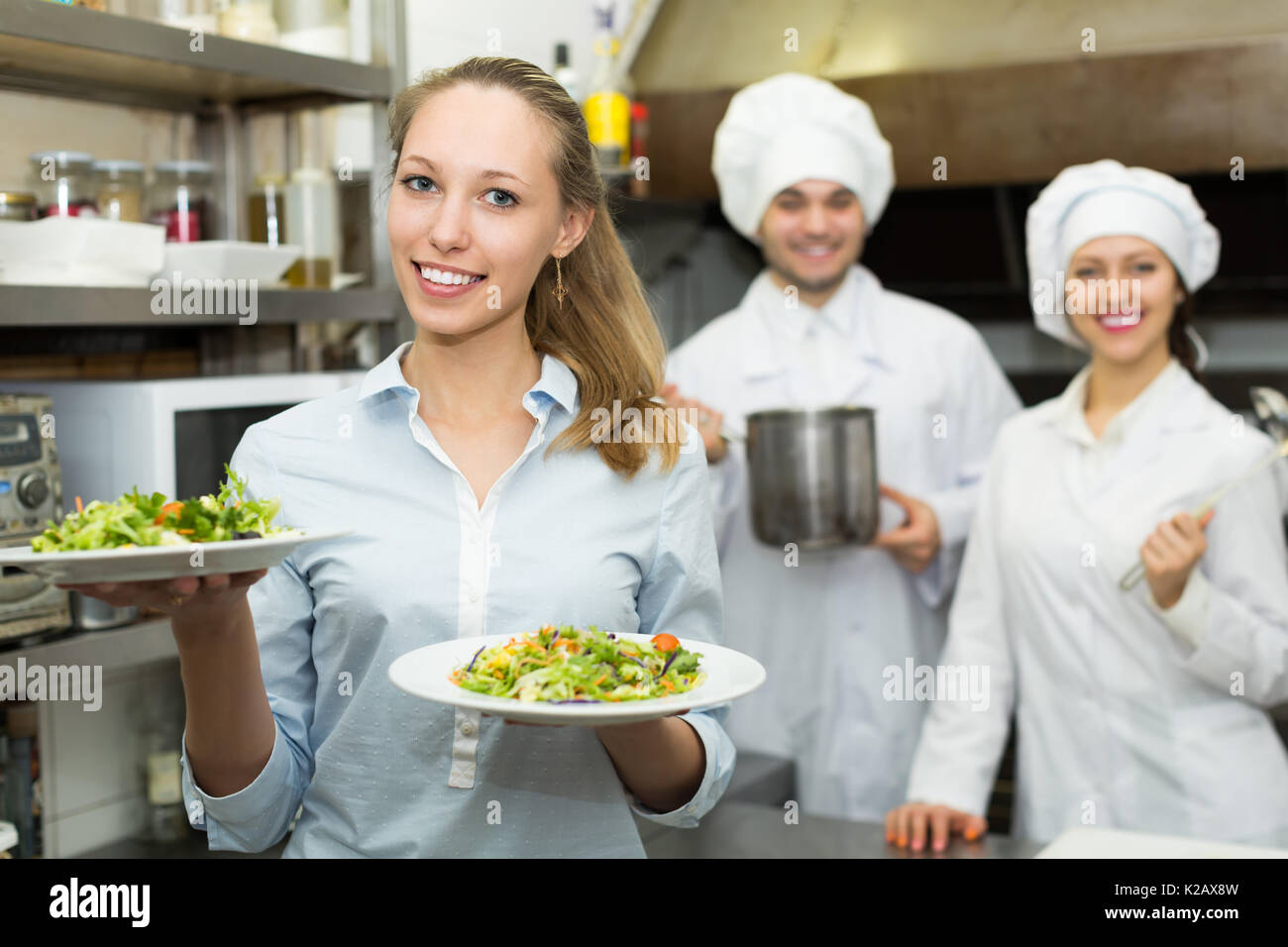 Young smiling waitress holding plates with meal and two cooks at ...