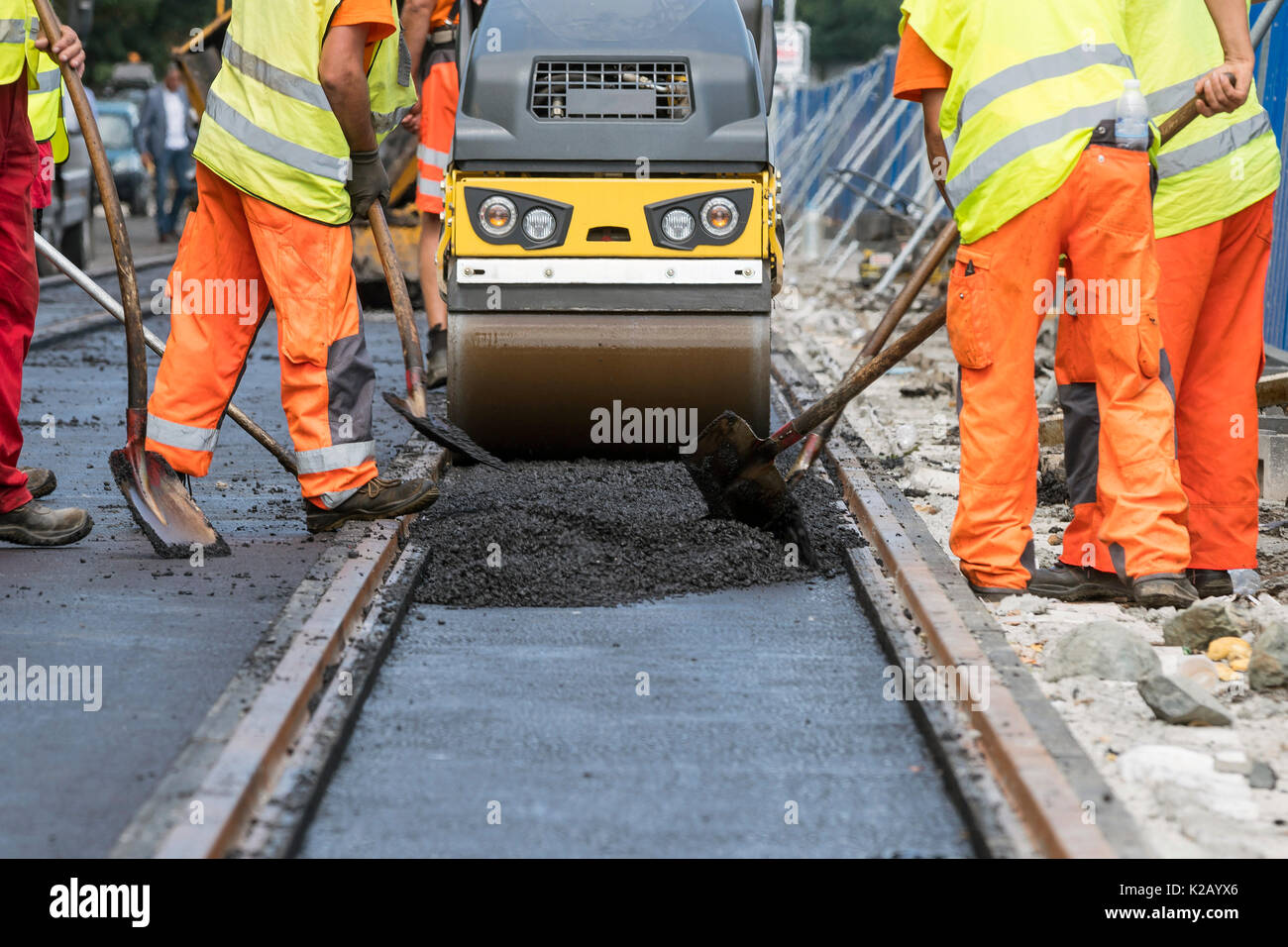 Team of workers put the hot asphalt on a street along tram car's ...