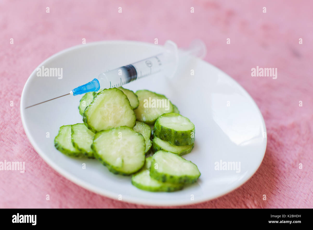 White plate with slices of green cucumber and a syringe with an ...