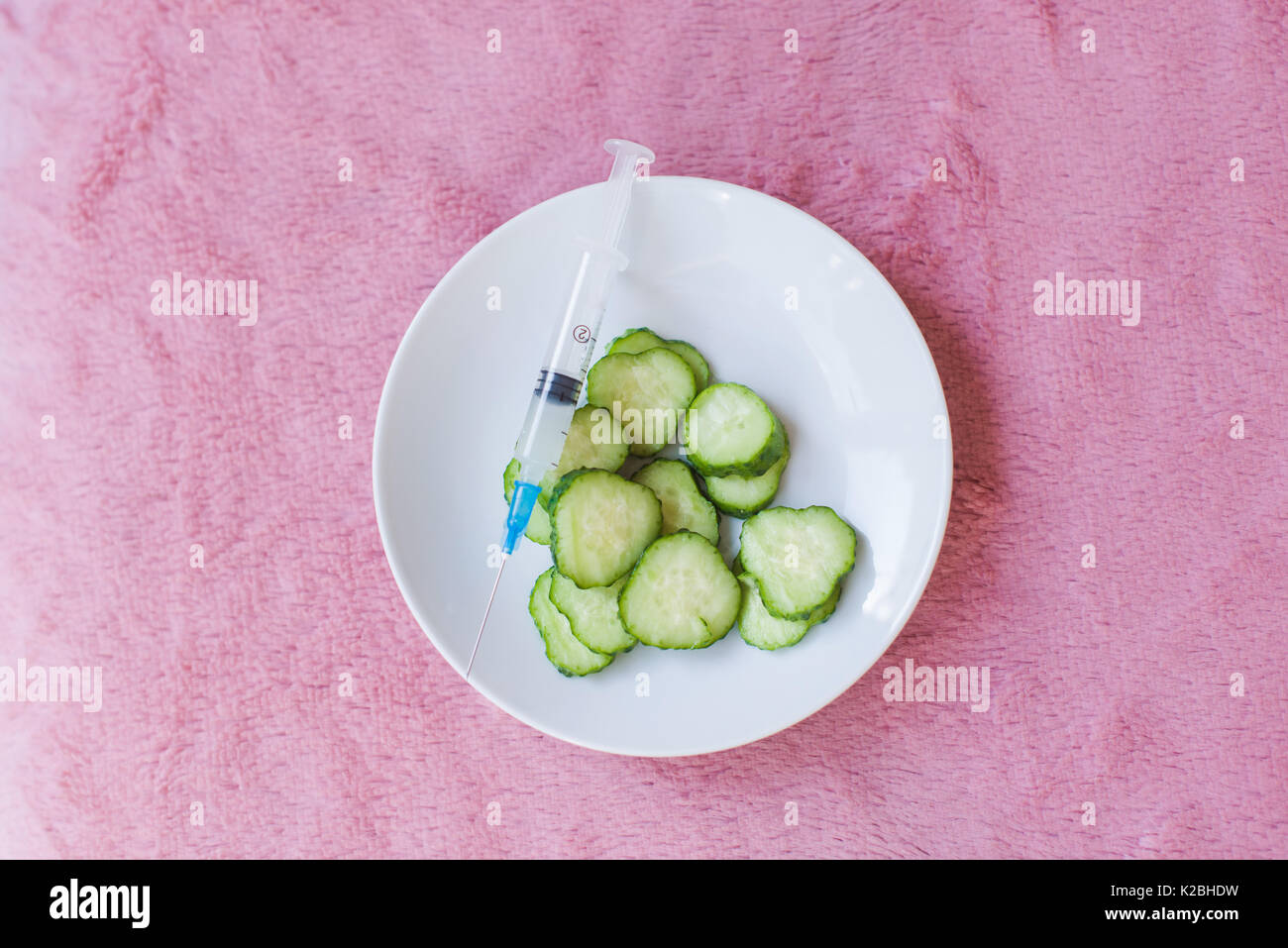 White plate with slices of green cucumber and a syringe with an ...