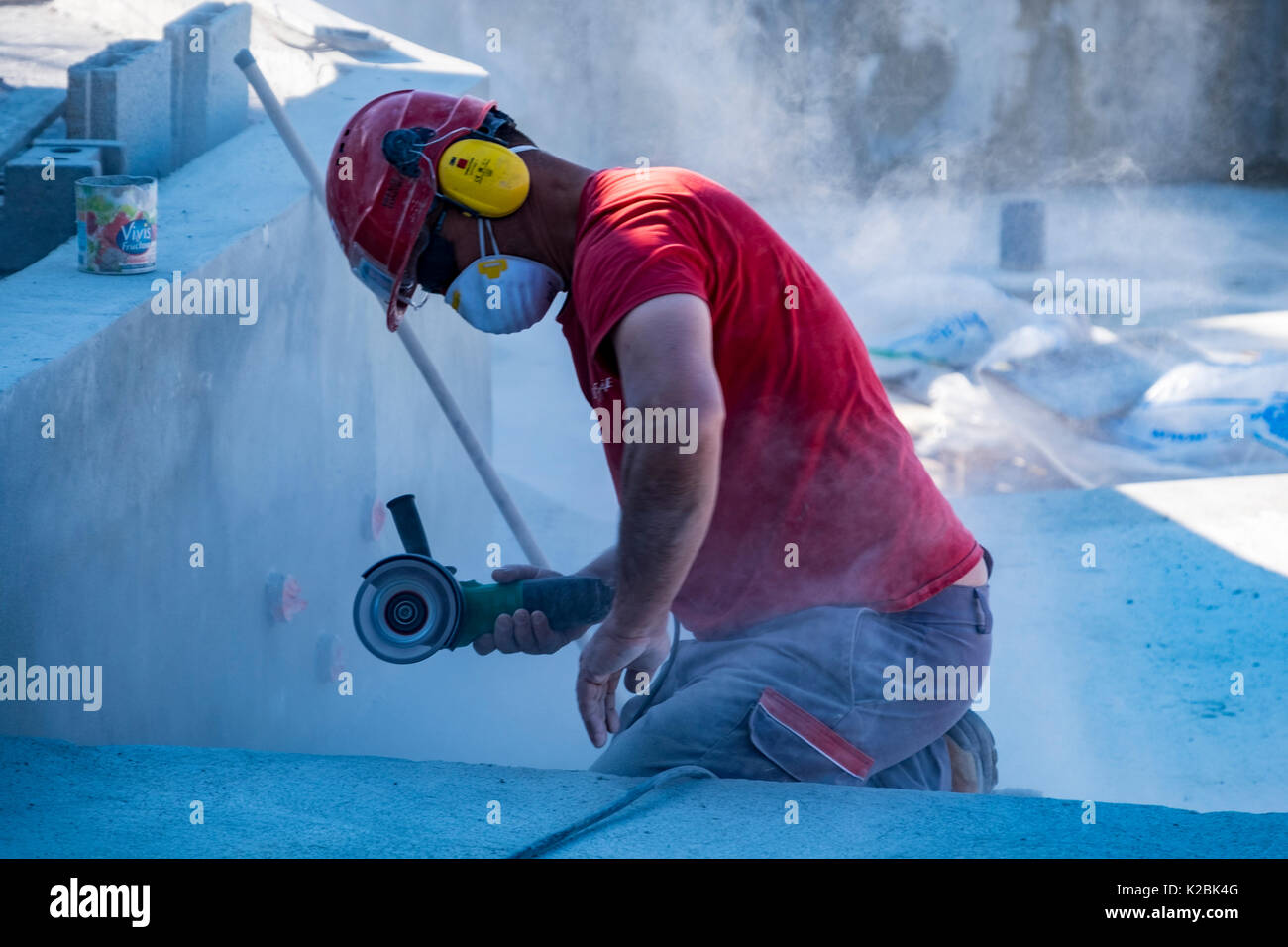 Construction worker wearing safety helmet and headphones uses a sander ...