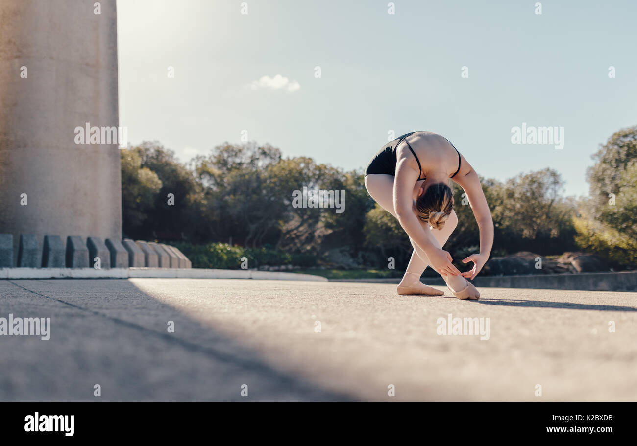 Ballet dancer practicing dance move outdoors. Dancer bending low in a ...