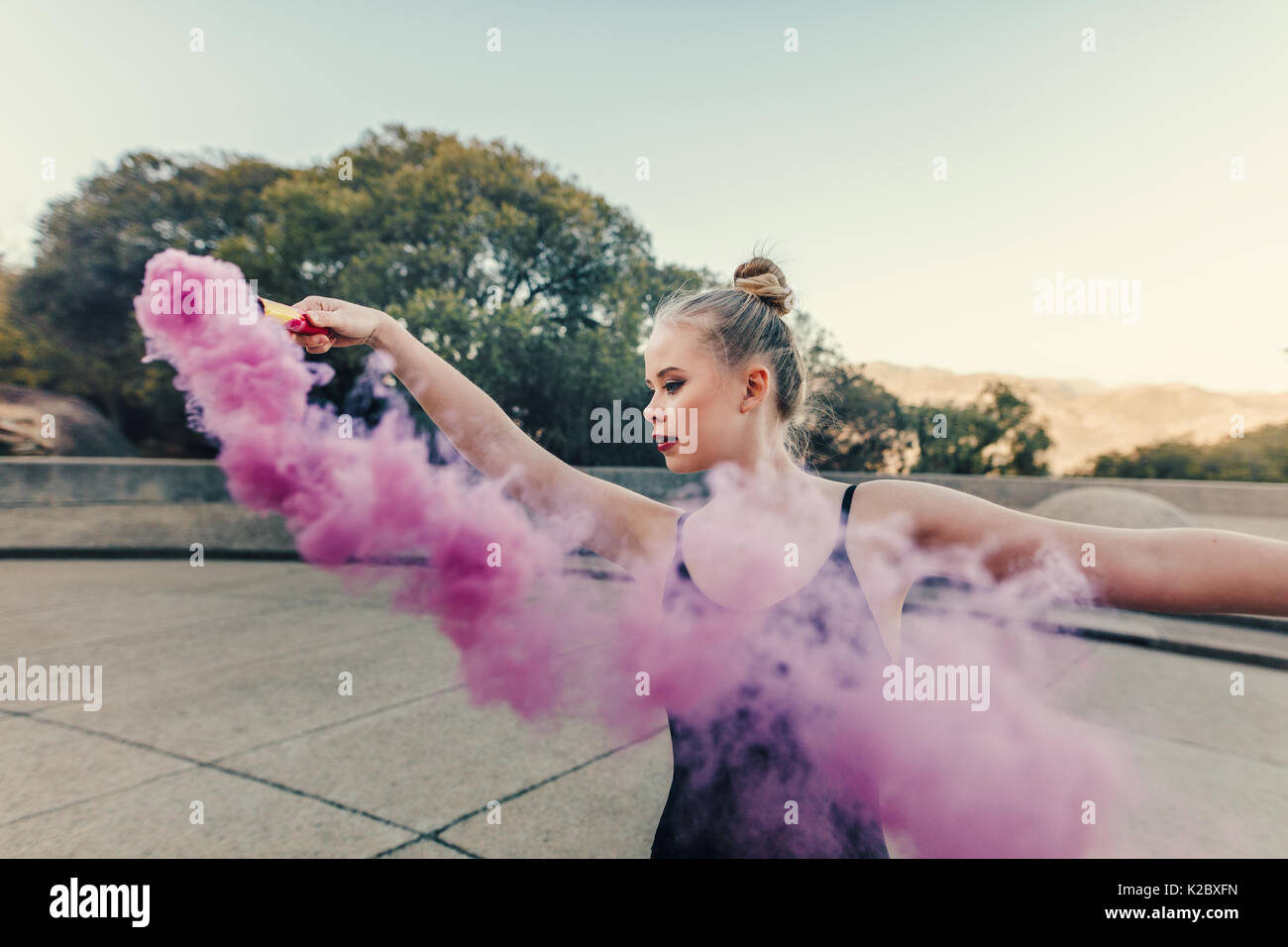 Ballet artist practicing dance moves outdoors using a pink smoke bomb ...
