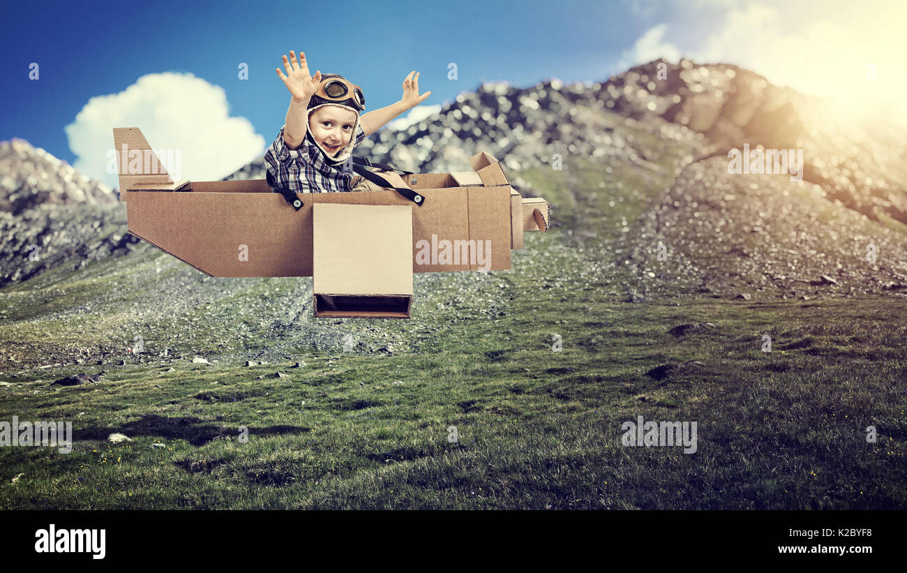 kid play aviator role on cardboard airplane with mountain background ...