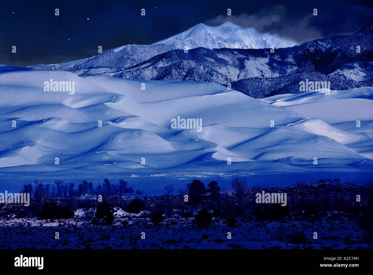 Moonlight reflects off the snow-covered sand dunes at night at the ...