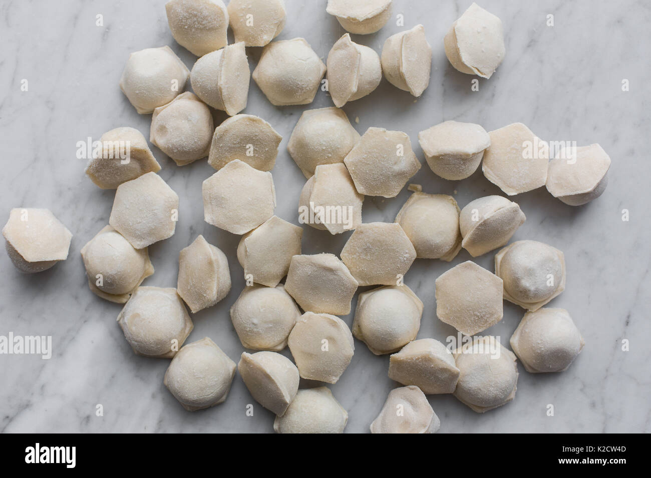 Raw frozen pastry dumplings close up over white rustic stone background ...