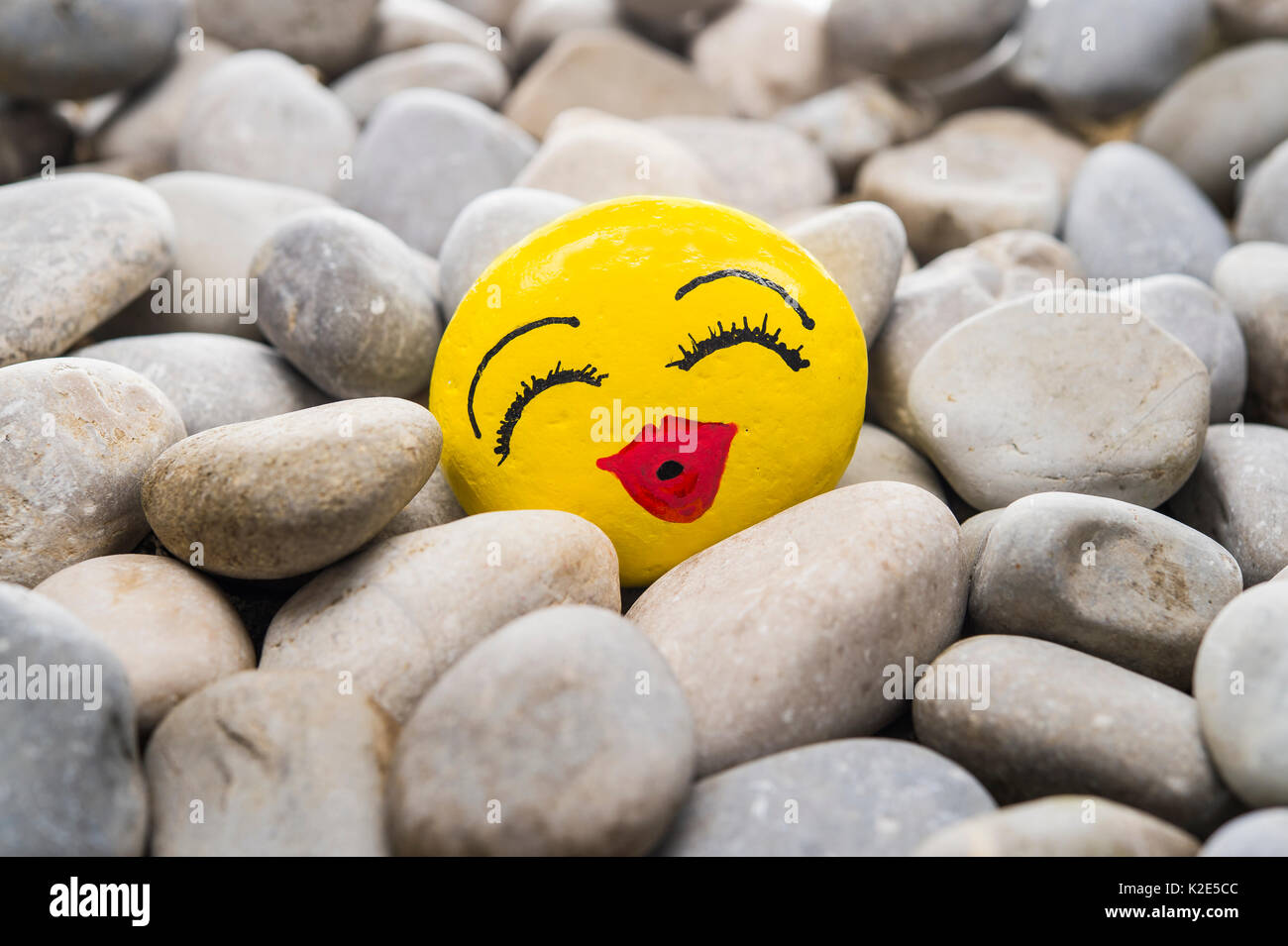 Smiley face made of stone, painted yellow with red kissing lips, lies ...