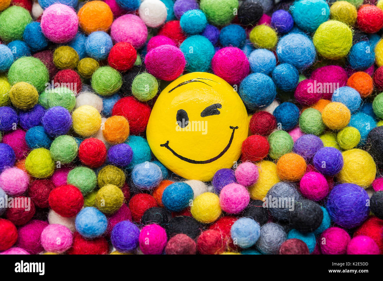 Smiley face made of stone, painted yellow, winking, lies in between ...