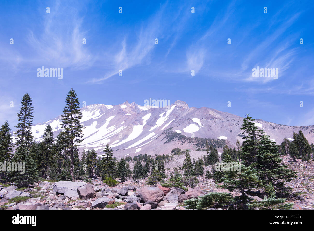 Mt. Shasta on a glorious sunny day is framed by fir trees on rocky ...