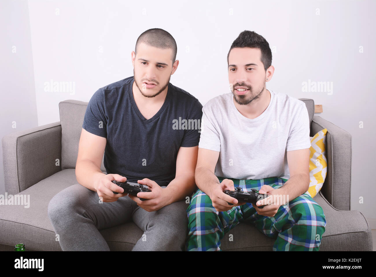 Portrait of two friends playing videogames and sitting on couch ...