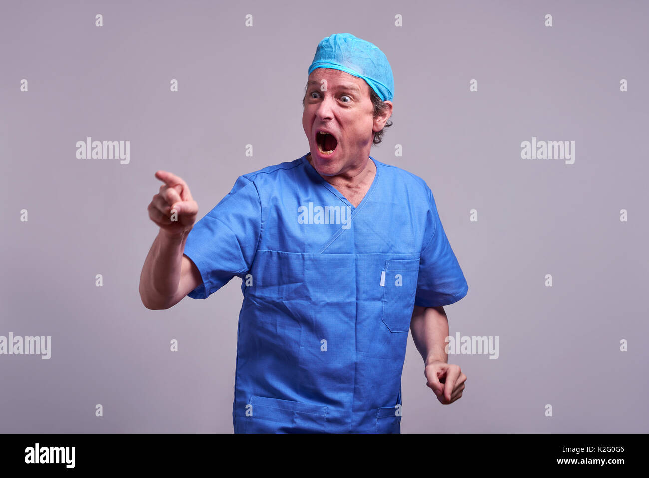 An angry middle aged male doctor standing in a blue scrubs and ...