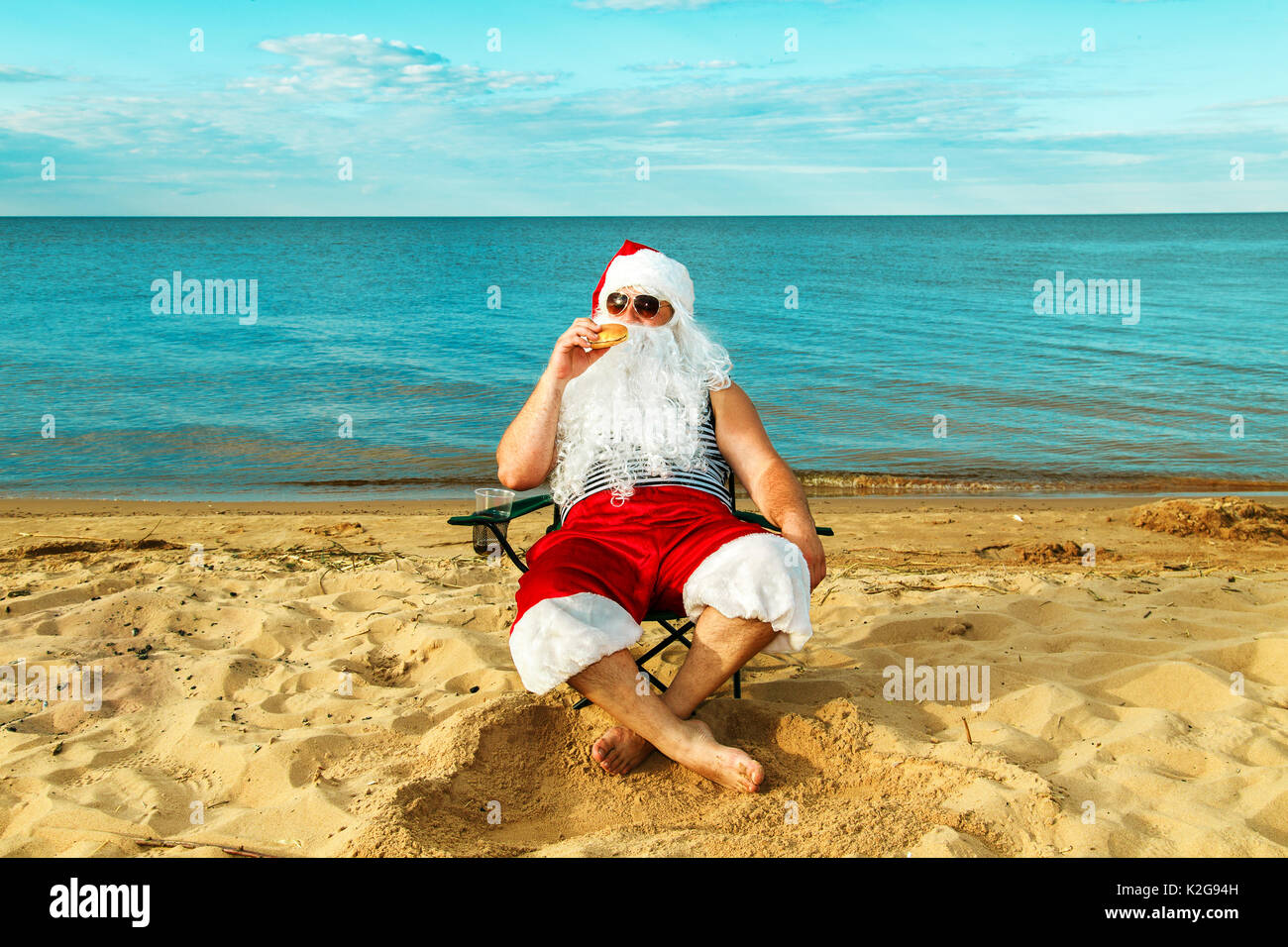 Santa Claus on the beach eating a hamburger. The concept of unhealthy ...