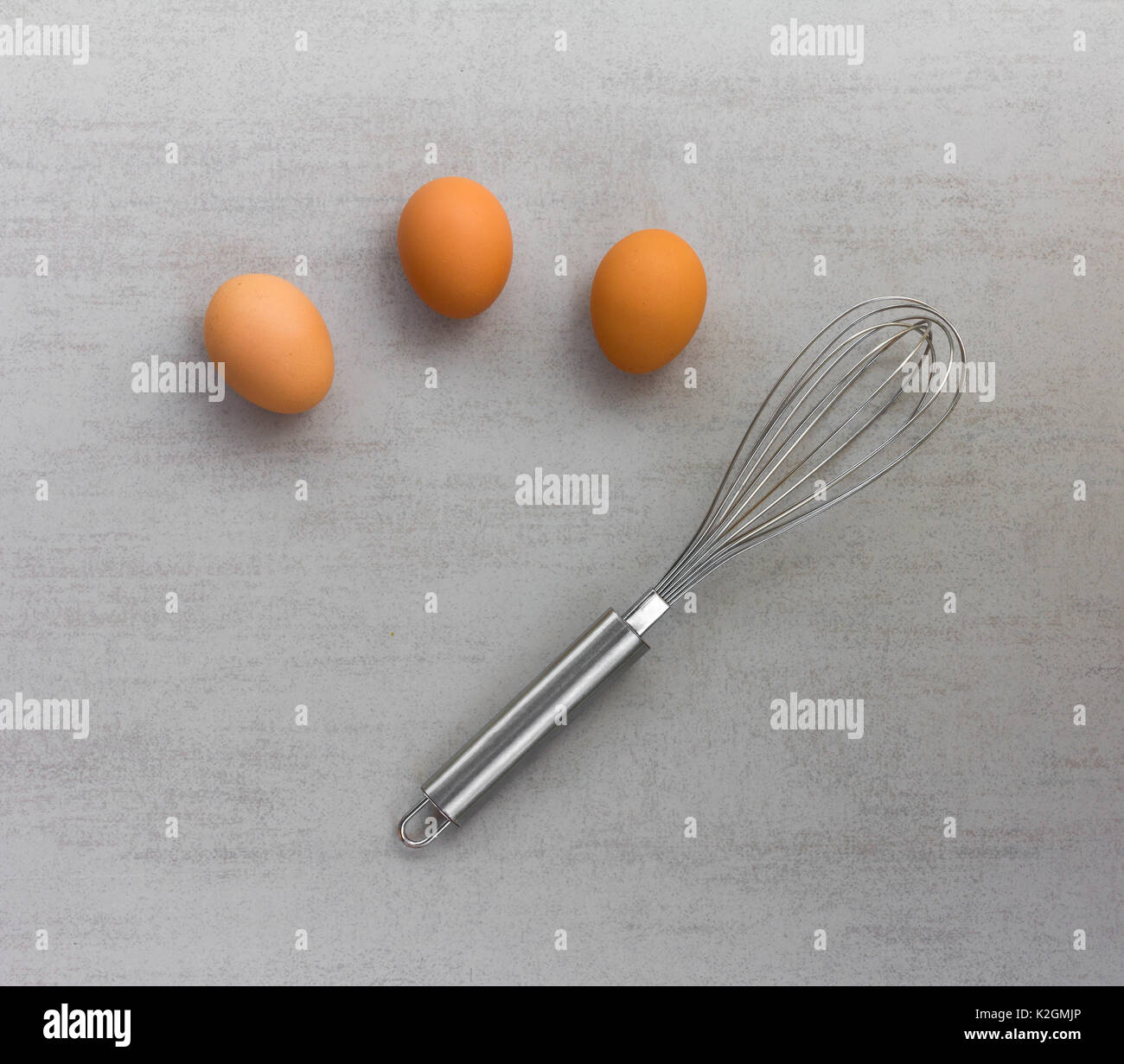 three chicken eggs and whisk on a steel gray background Stock Photo - Alamy