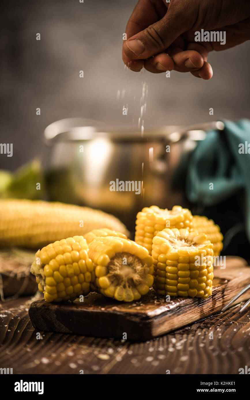 Hand salting hot cooked corn on the cob. Serving cooked autumn snack ...