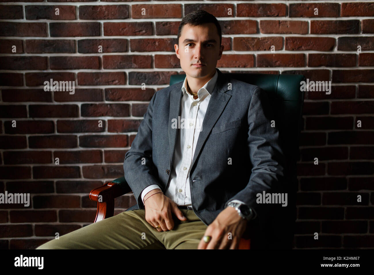 Photo of brunet in jacket sitting on chair against brick wall ...