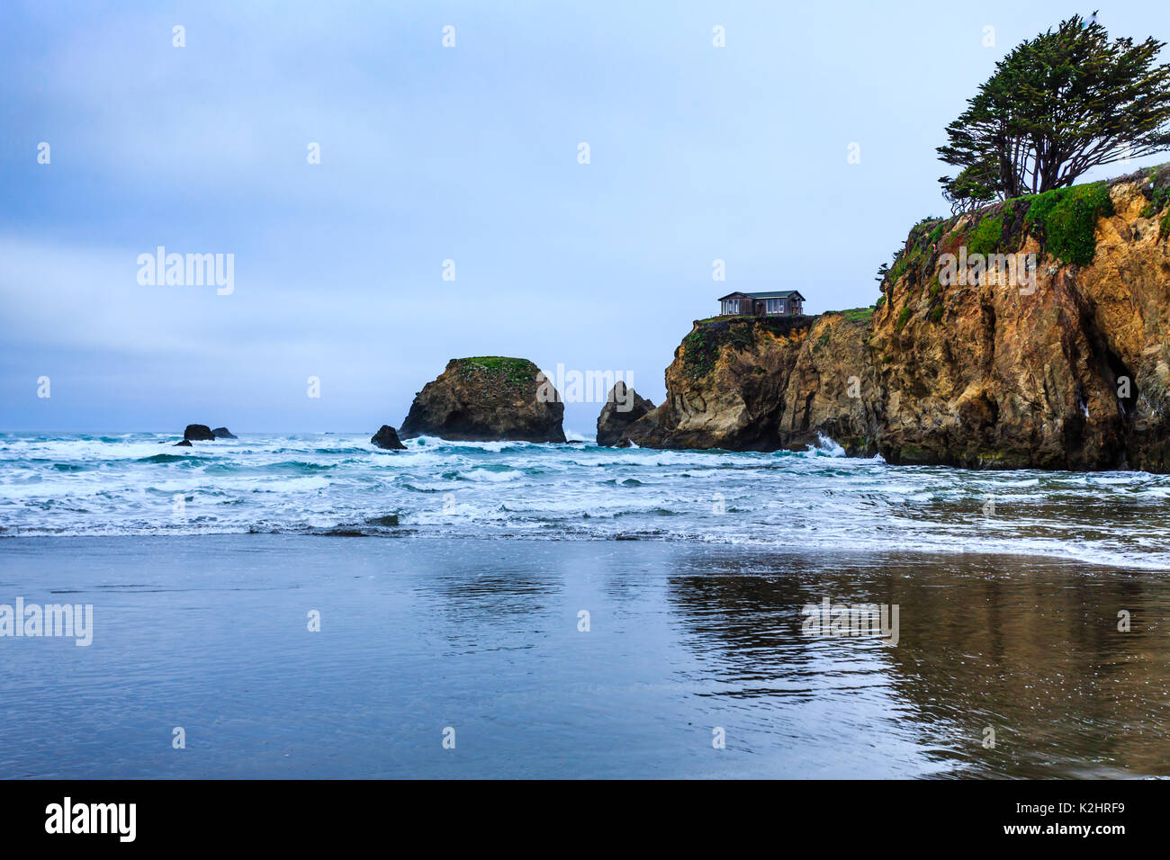 Cliff at the end of the beach has single house and single tree on top ...