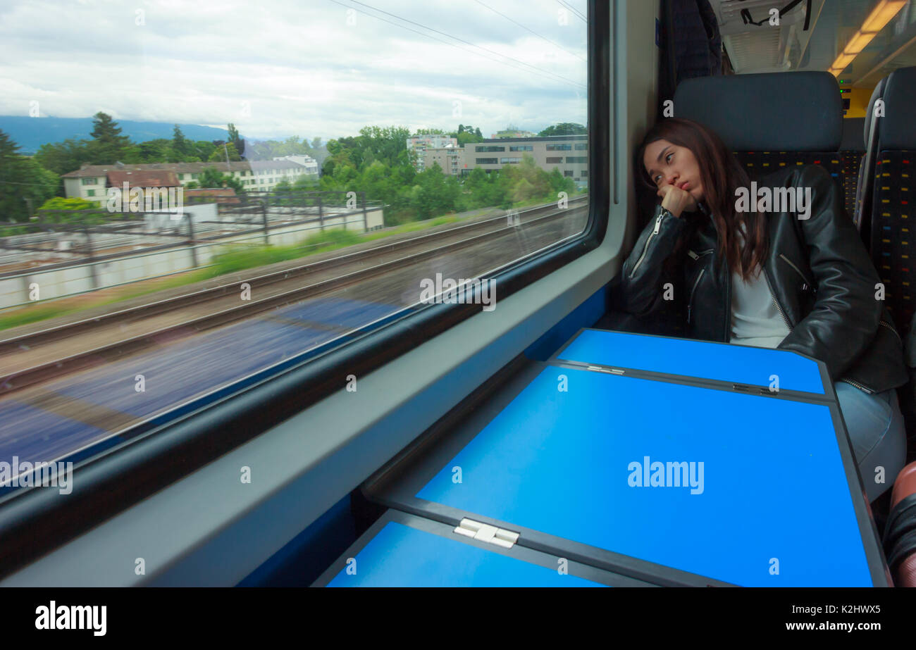 Asian woman looks outside of the train's window, looking bored or tired ...