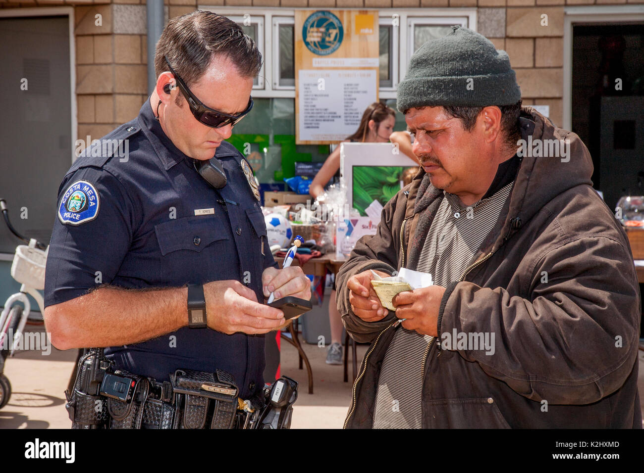 A policeman in a Costa Mesa, CA, park advises a homeless Hispanic man ...