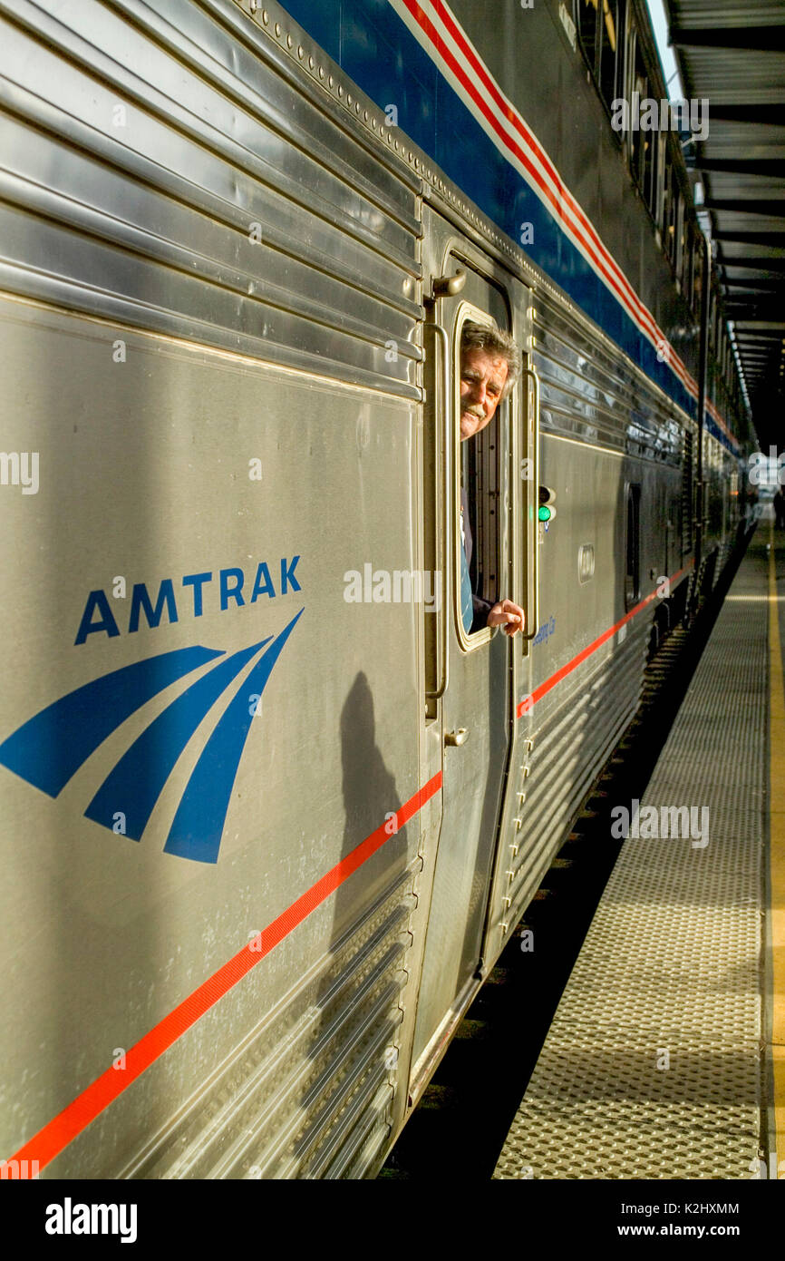 In bright afternoon sunlight, a middle-aged railroad conductor smiles ...