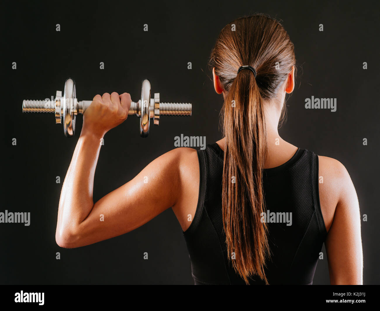 Photo of the back of a young woman doing a shoulder press with a ...