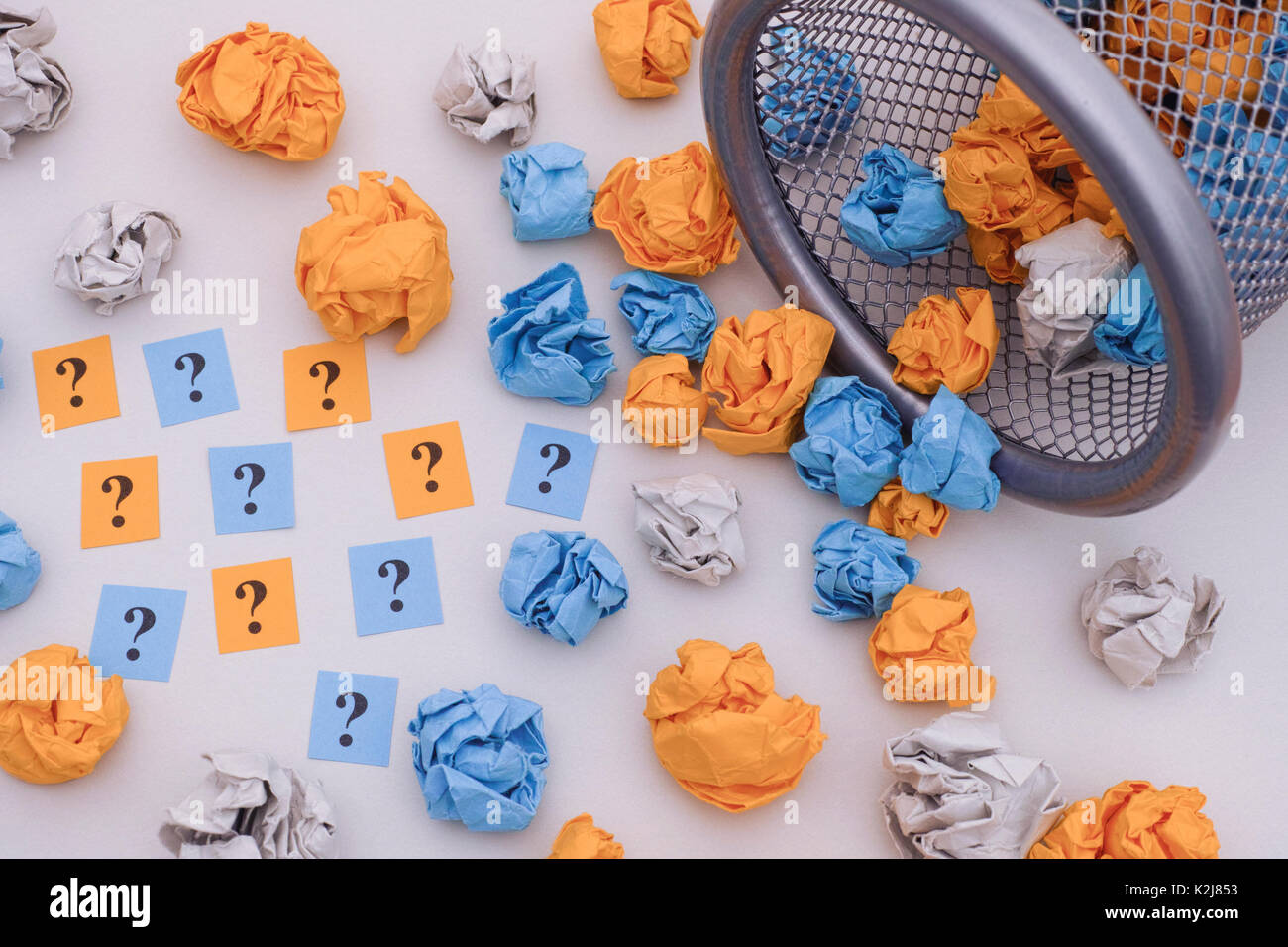 Colorful crumpled paper balls and question marks rolling out of a trash ...