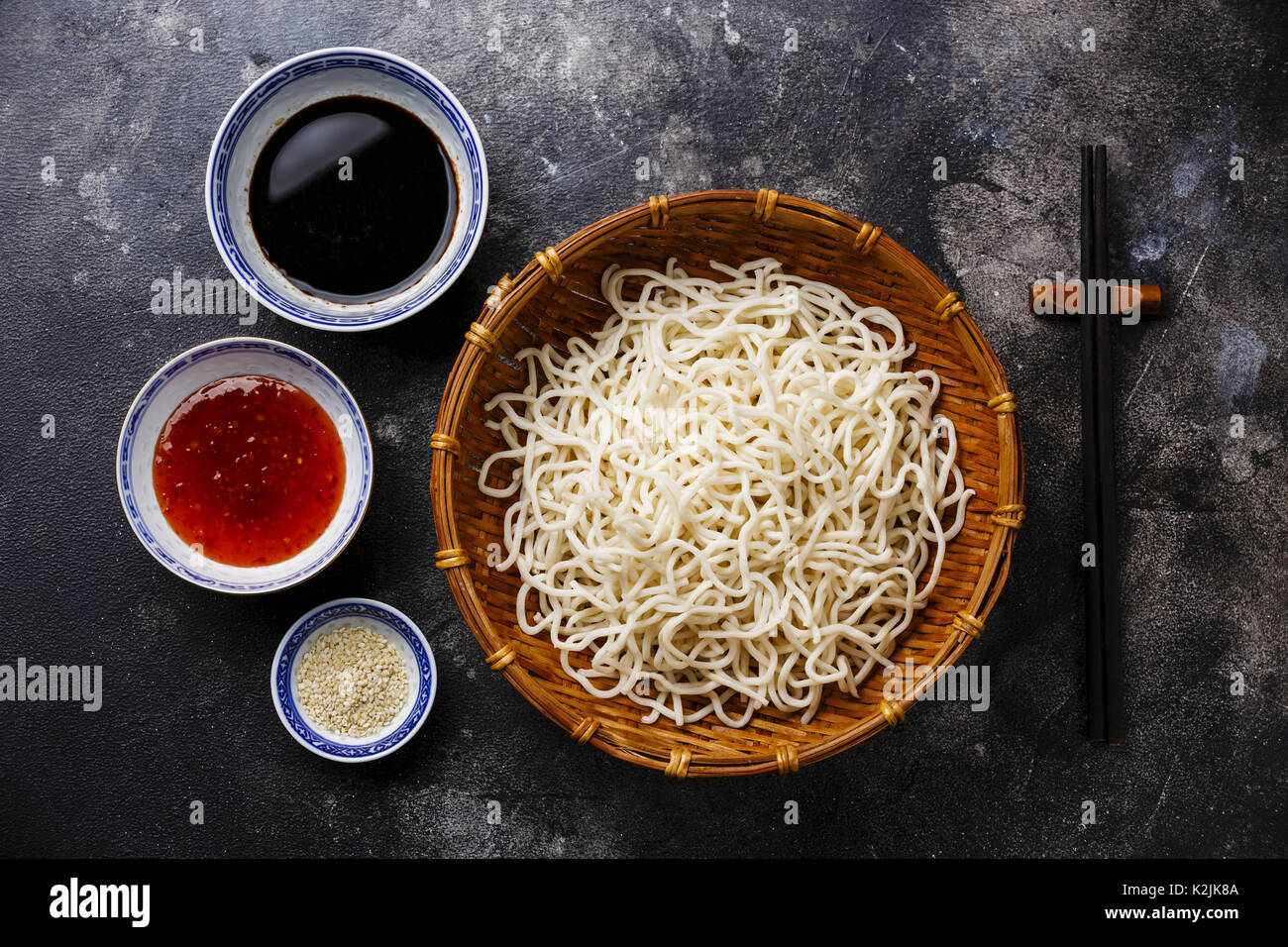 Raw Udon noodles in bamboo basket with sauces and sesame on dark ...