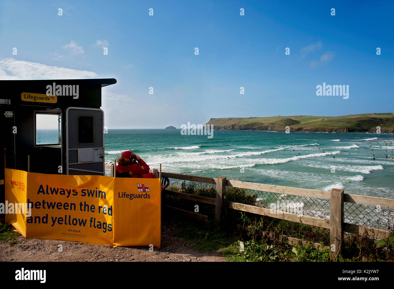 A RNLI lifeguard keeping watch with binoculars over the surfers and ...