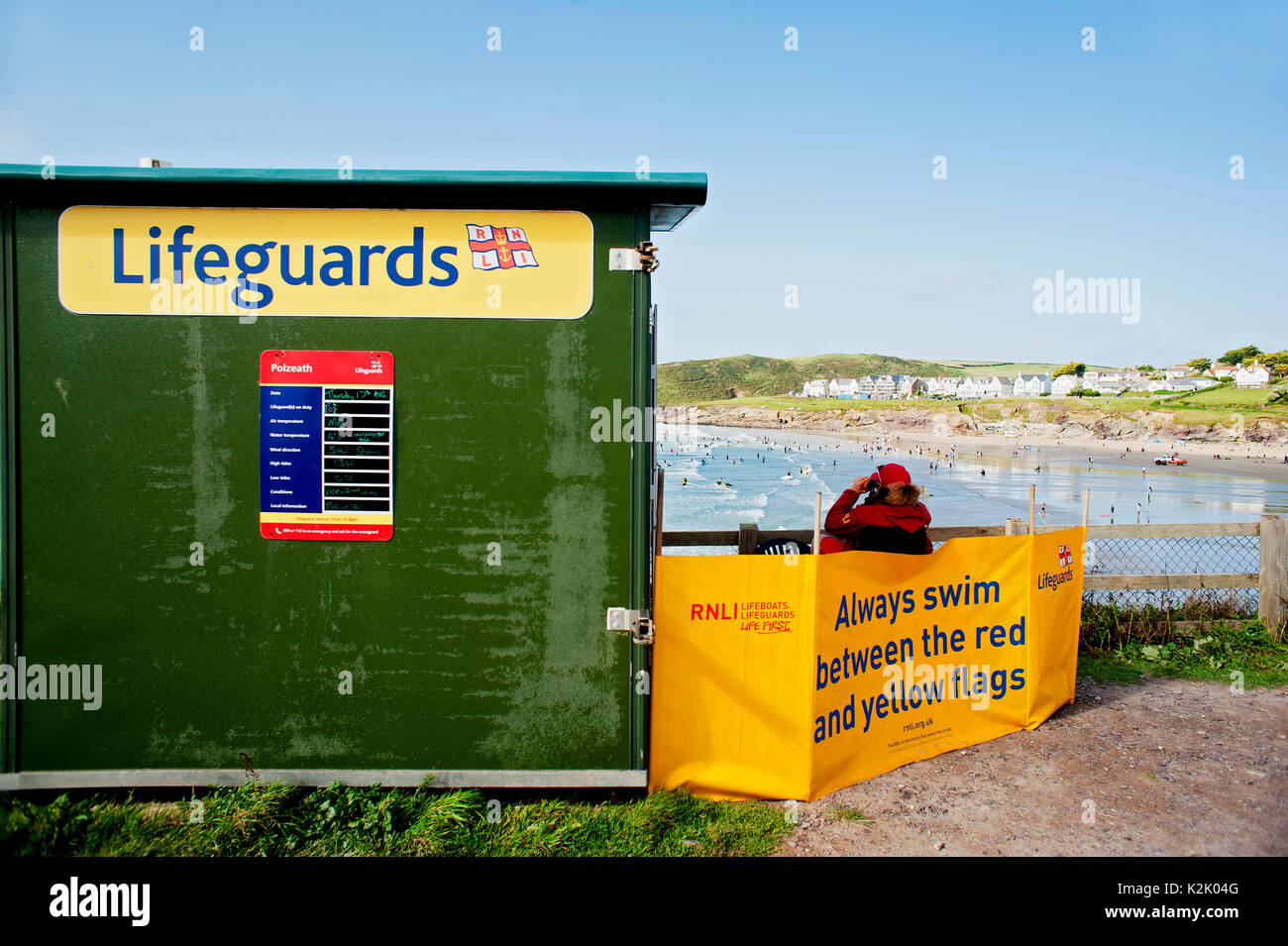 A RNLI lifeguard keeping watch with binoculars over the surfers and ...