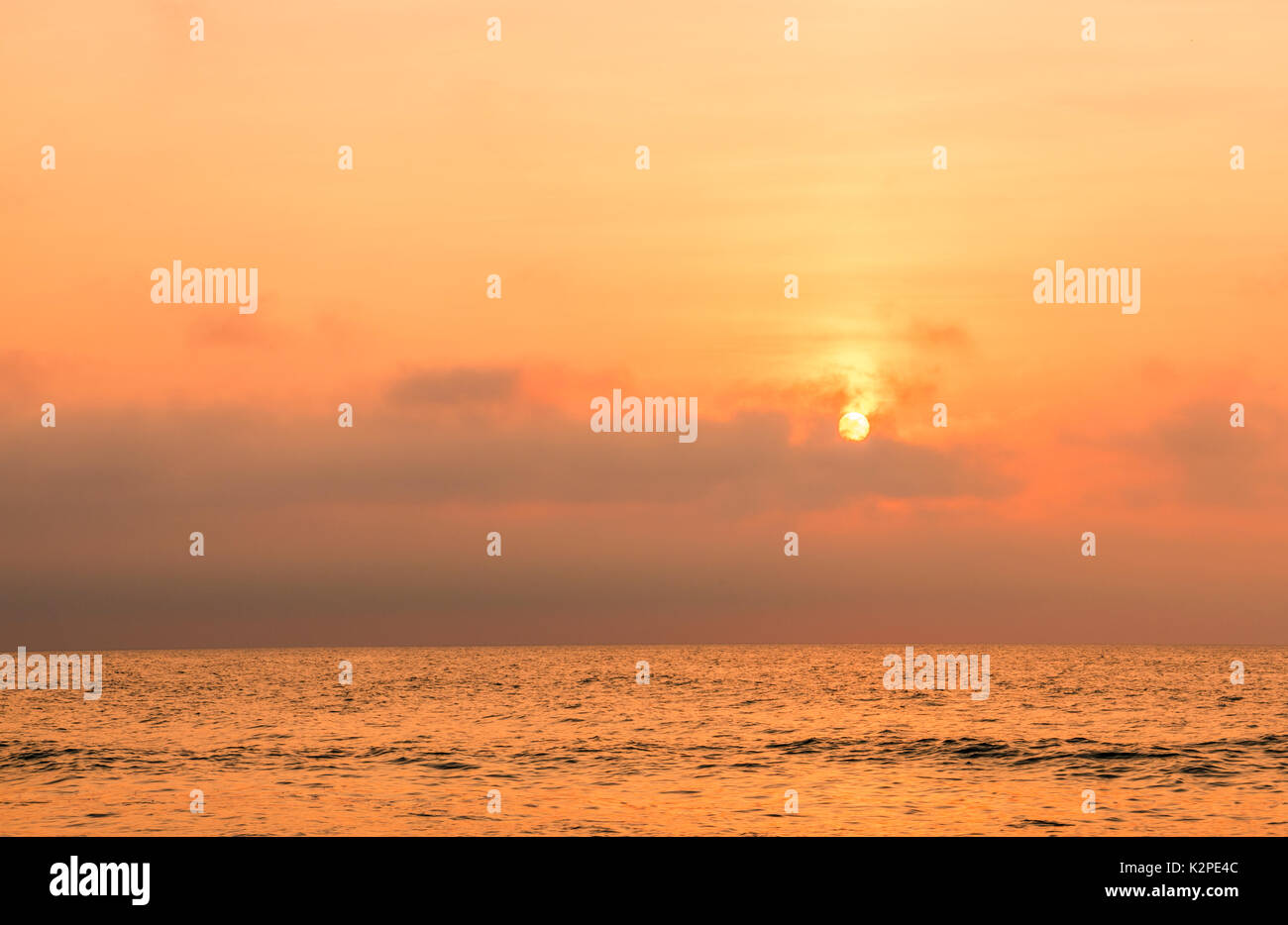 Golden color ocean on the foreground and cloudy sky with partly hidden ...