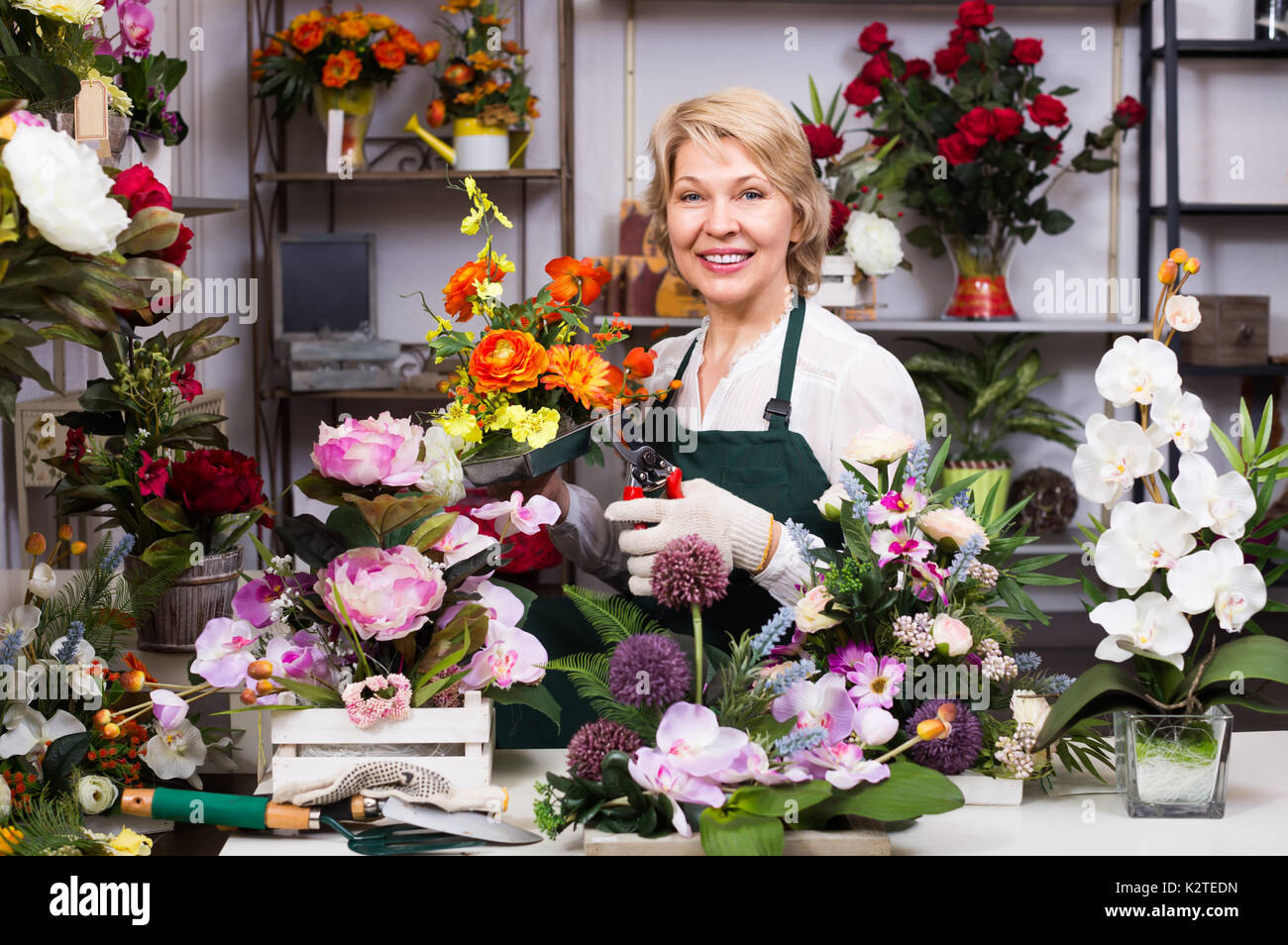 Portrait of smiling mature woman florist with clippers making flowers ...