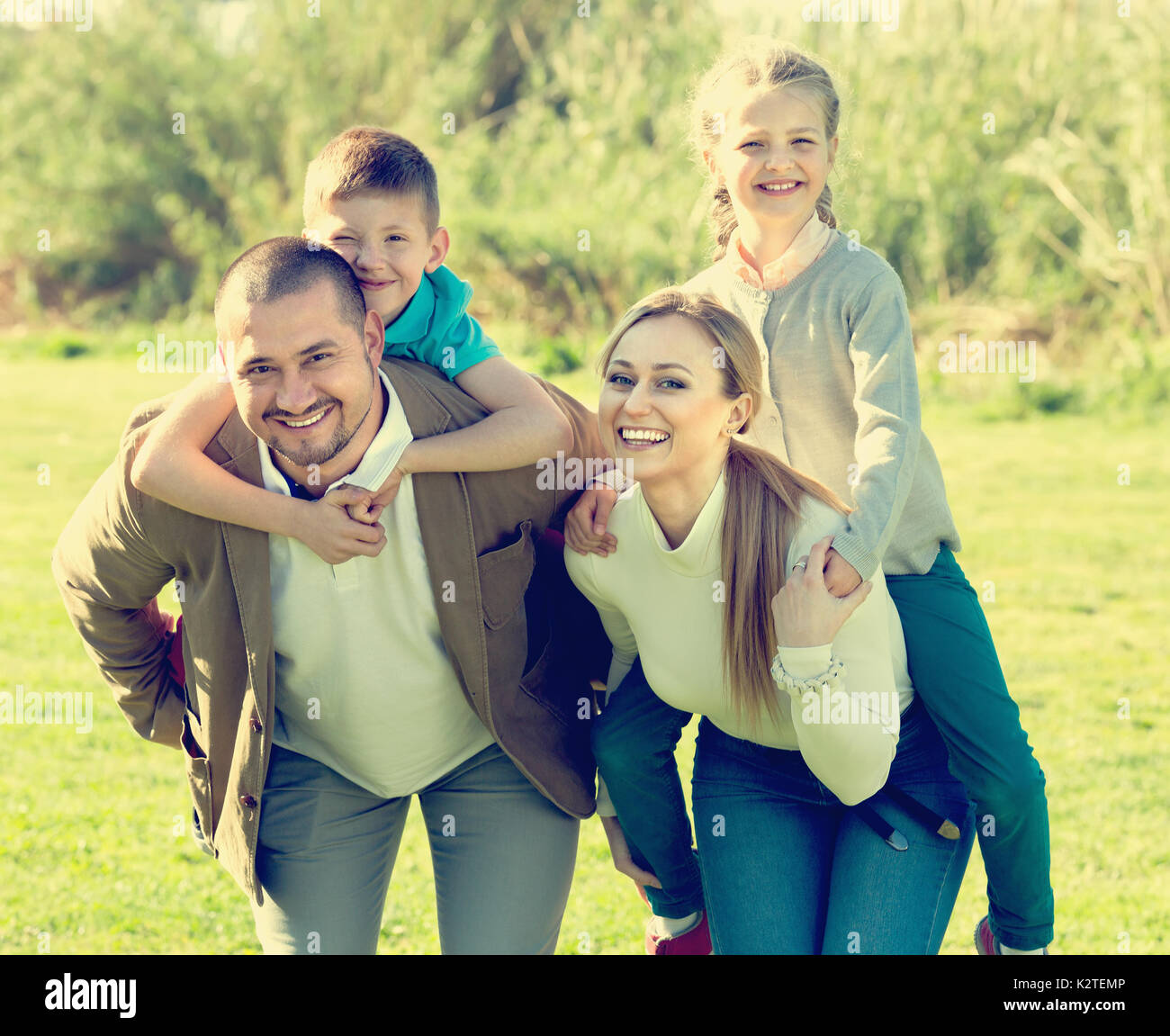 Happy mother and father carrying two children on the back in the park ...