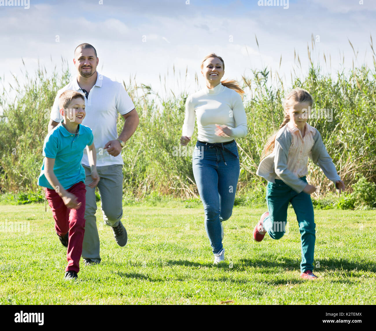 Cheerful young parents with two kids playfully running on the green ...