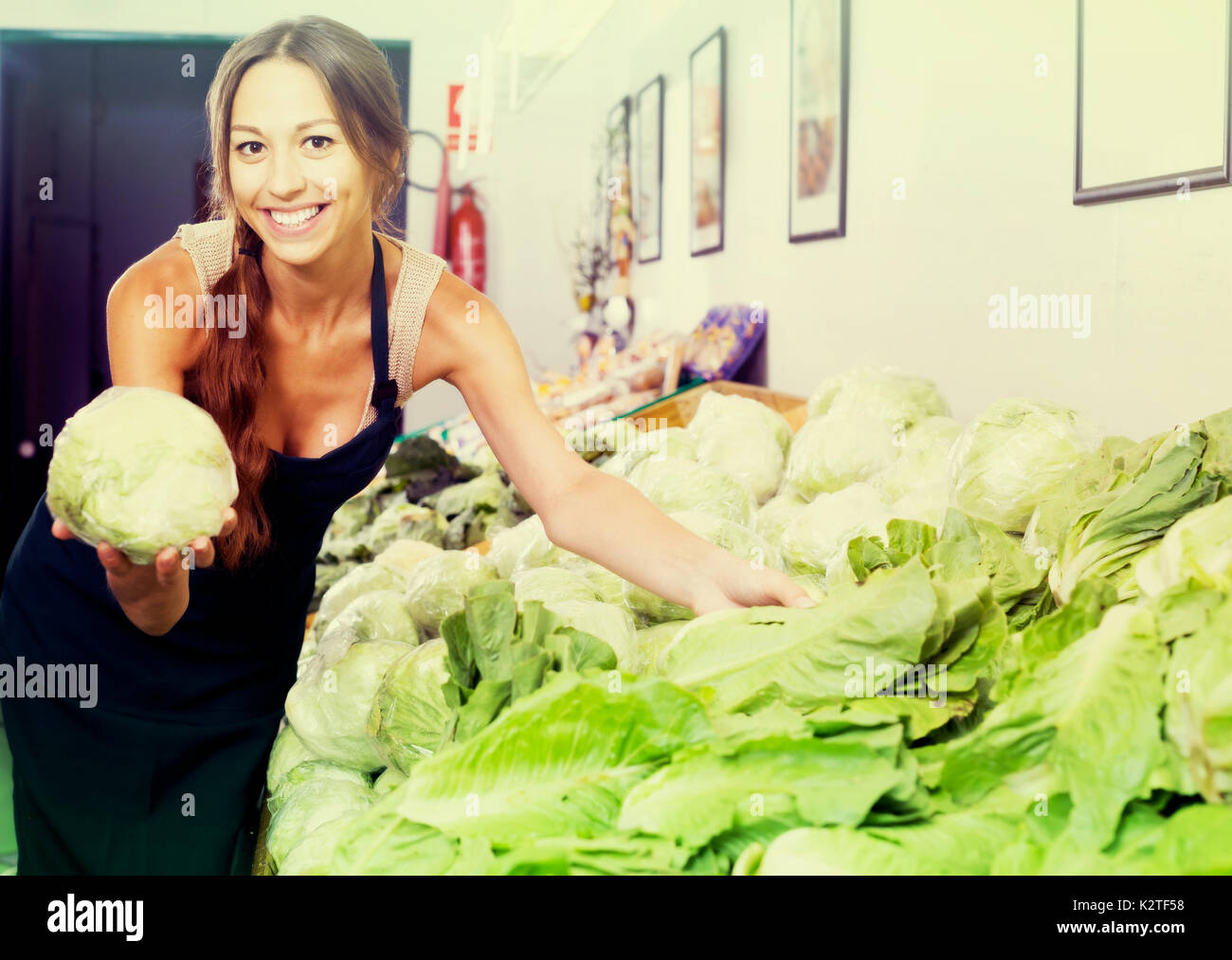 Happy young female seller wearing apron holding fresh cabbage head on ...