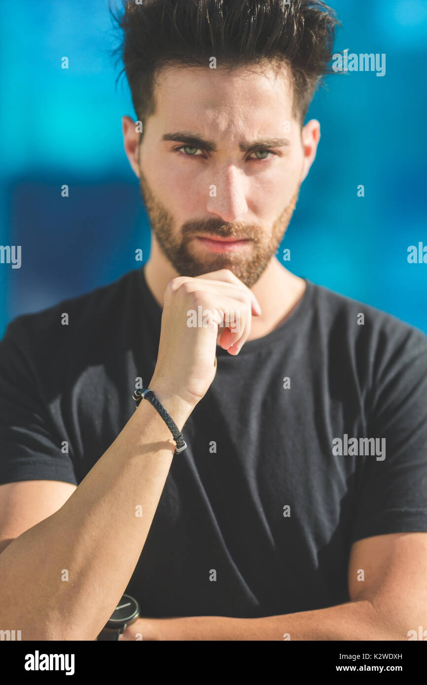 Front portrait of young man propping chin on hand frowning forehead ...