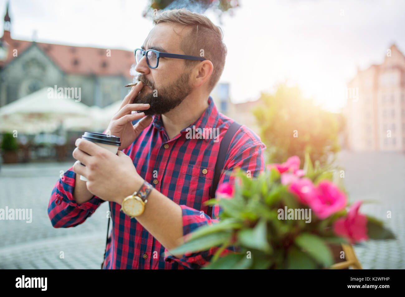 Man sitting in cafe garden and smoking cigarette in morning sunlight ...