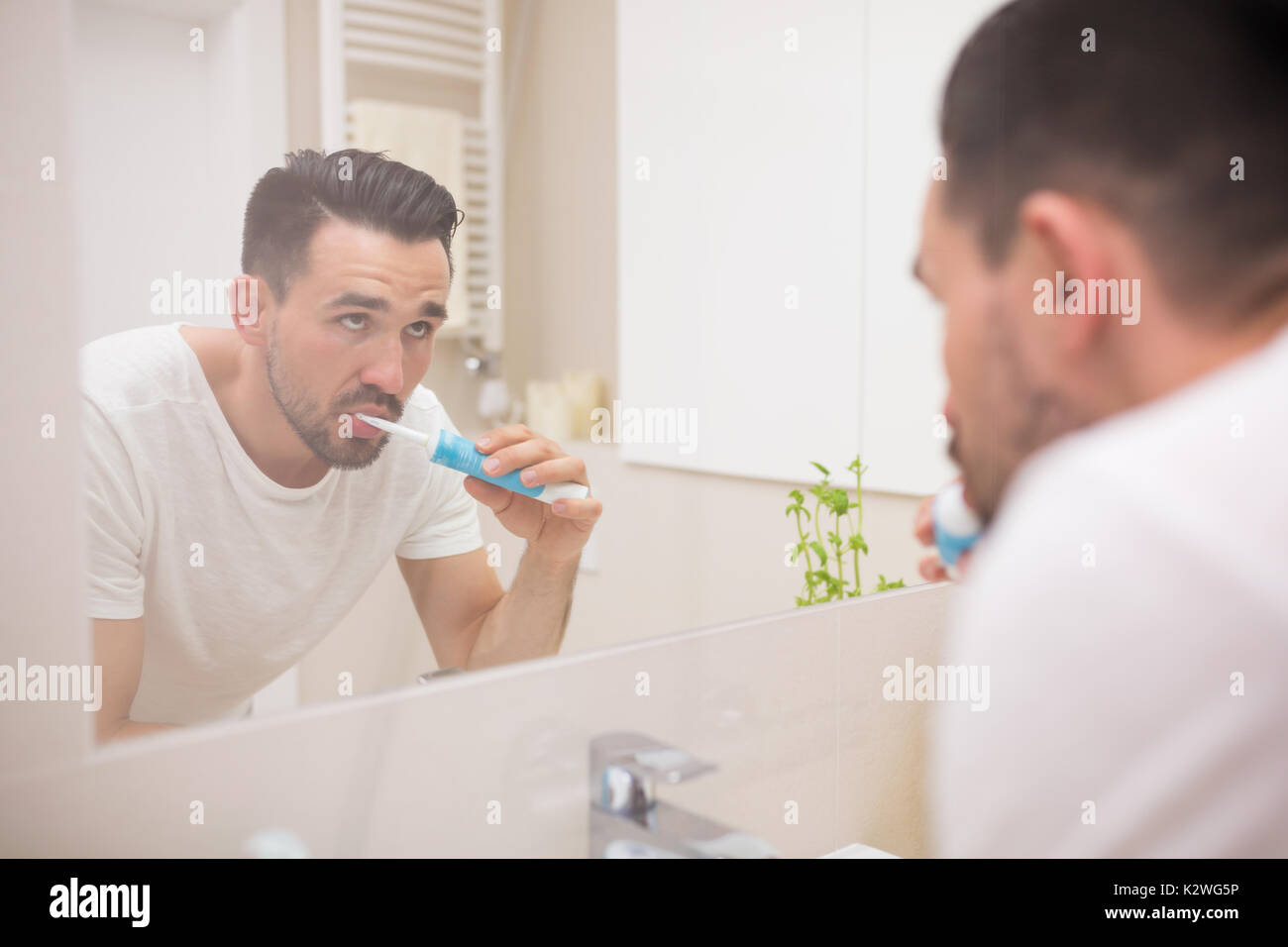 Reflection of an attractive man brushing teeth with an electric ...