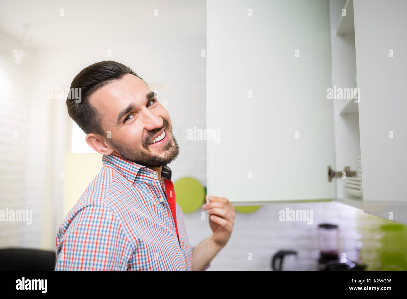 Smiling man standing in kitchen by the closet. White modern kitchen ...