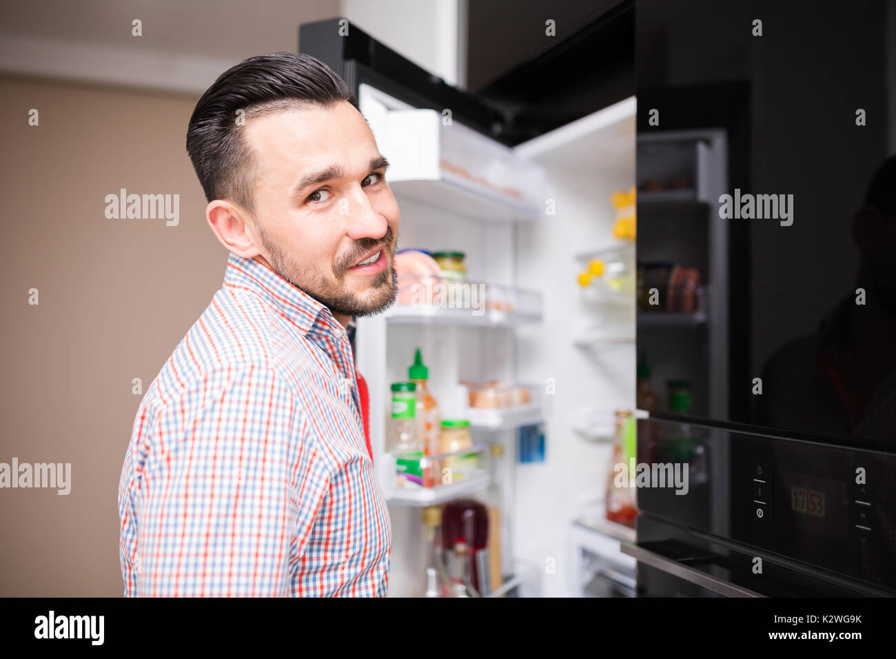 Handsome bachelor opening his modern fridge. Black kitchen furniture ...
