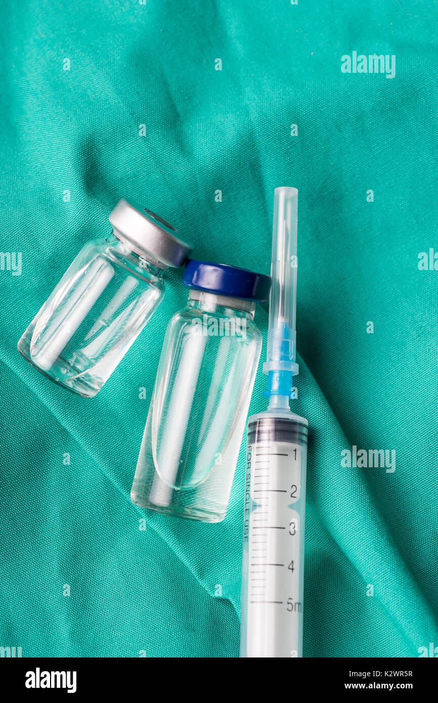 Medical syringe and vials lying on the hospital's green background. The ...