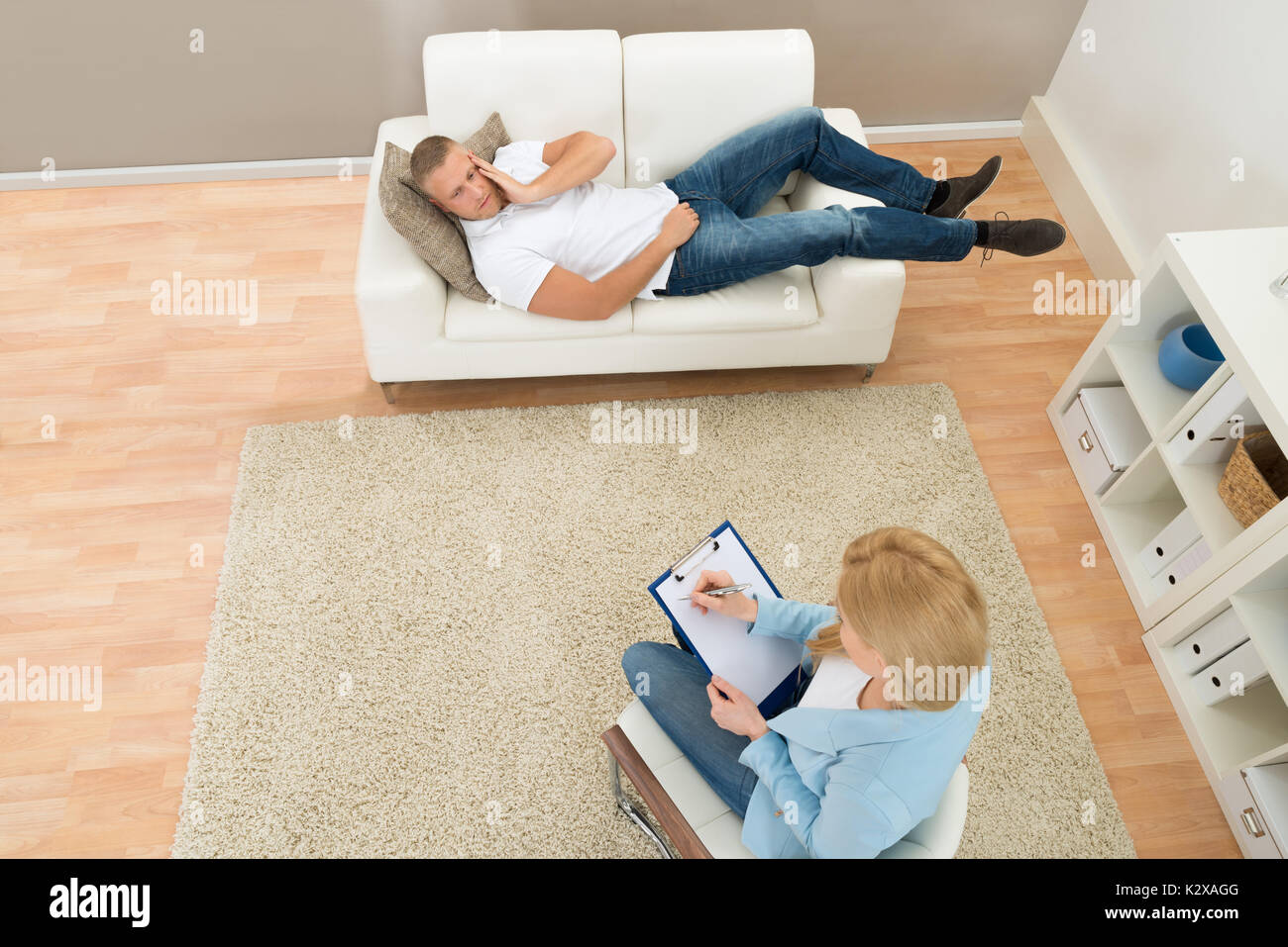 Patient Lying On Couch In Front Of Psychiatrist Writing On Clipboard ...