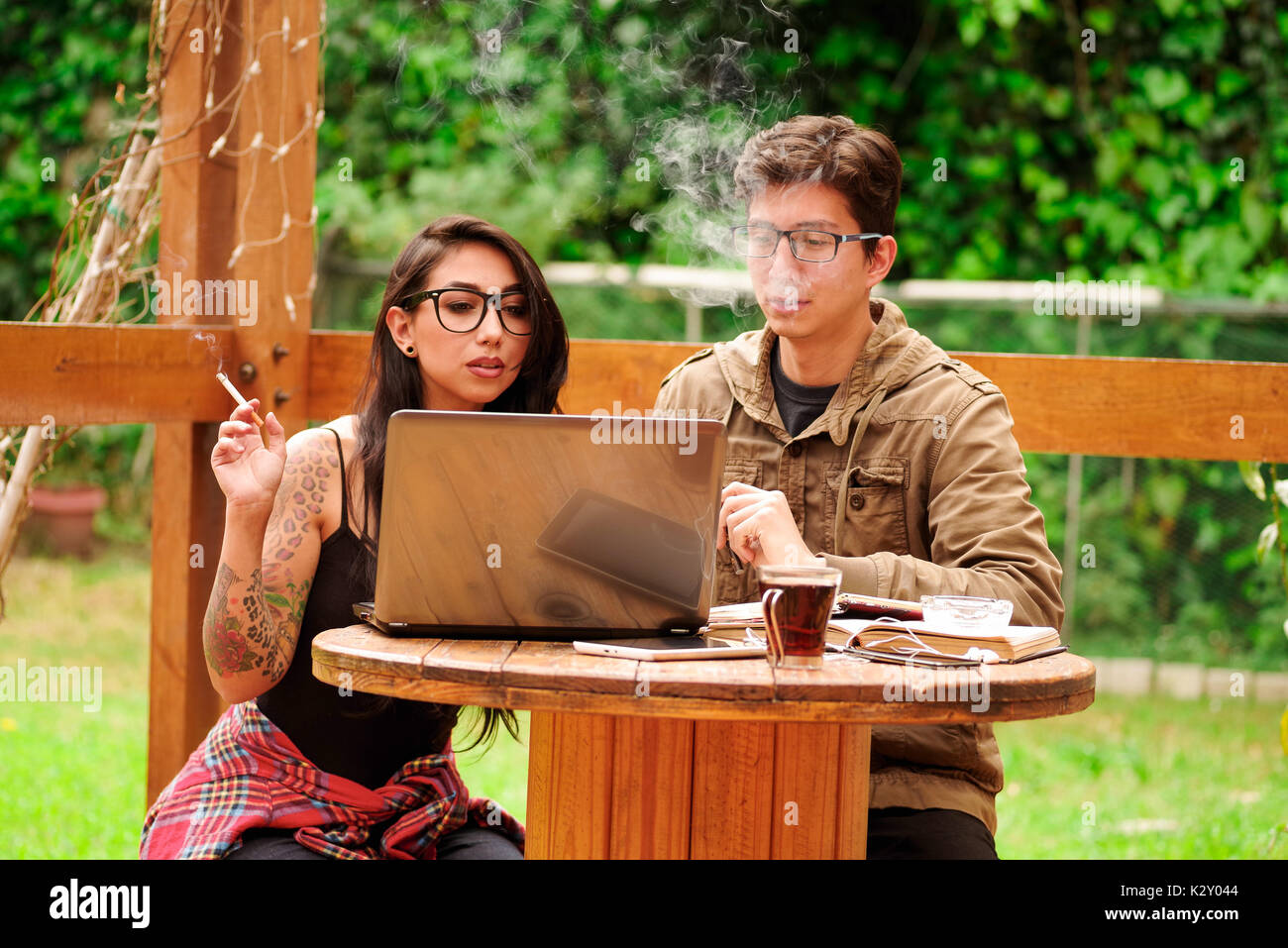 Hipster couple smoking and working on porch of wooden house, romantic moment, summer relaxing ...
