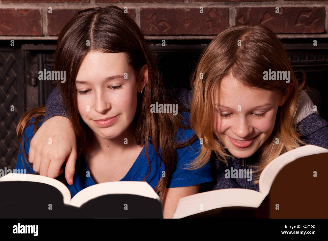 Two sisters reading books together with arms around their shoulders ...