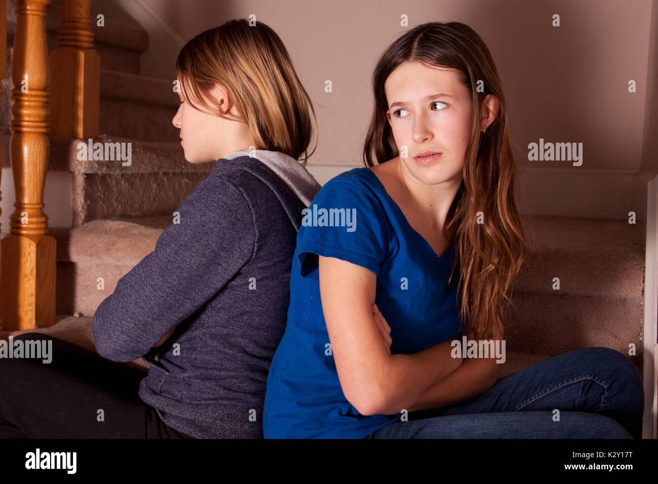 Two teenage girls sitting on the stairs back to back looking angry with ...