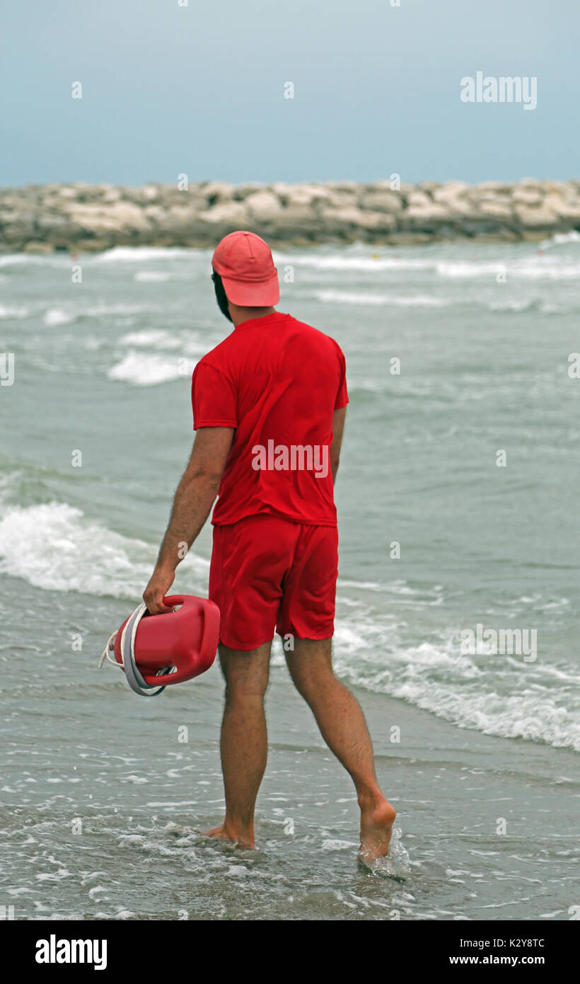 muscular lifeguard with red uniform checking the coast during storm in ...